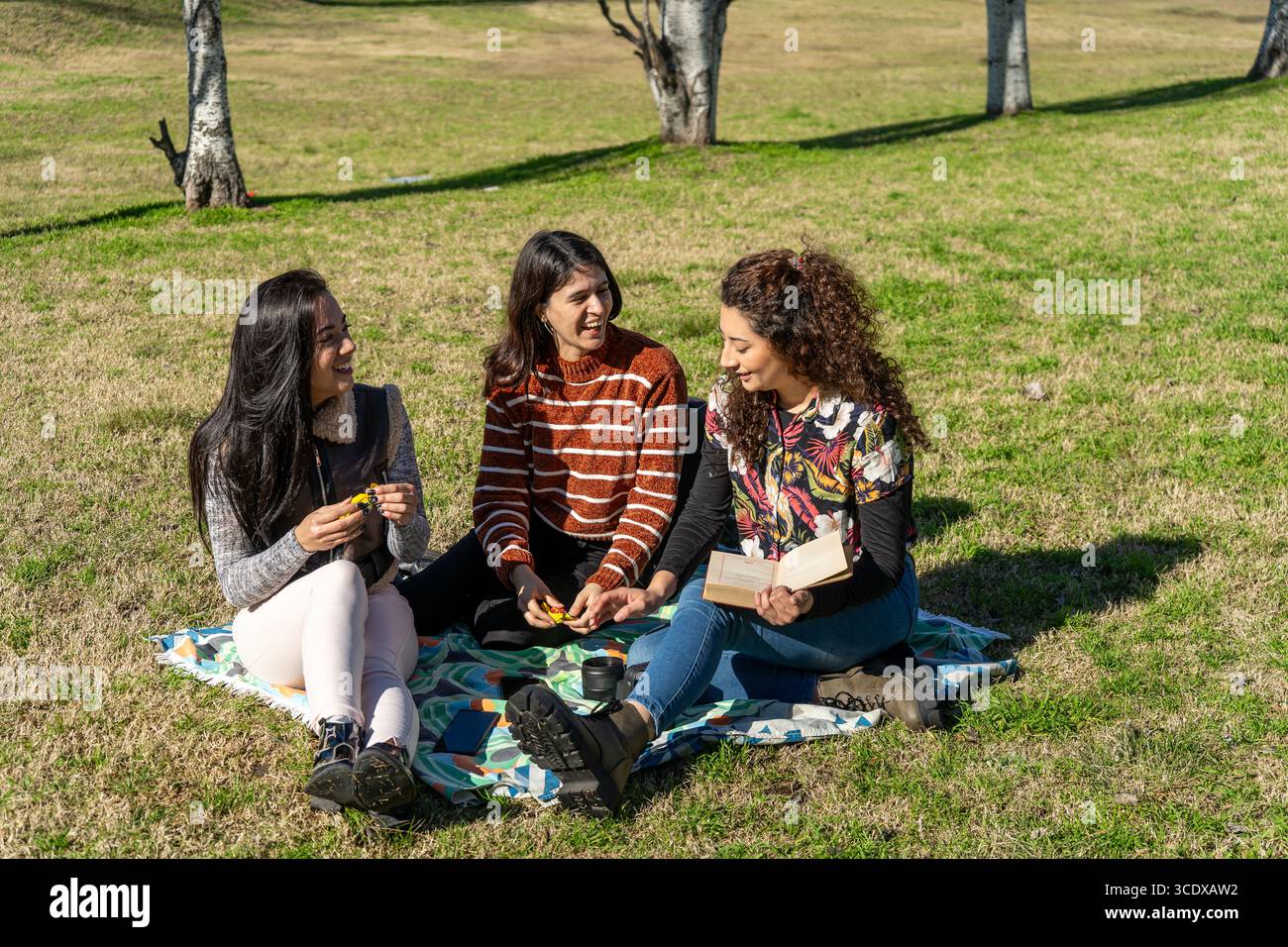Three cheerful latin friends are lying on a blanket, laughing and ...