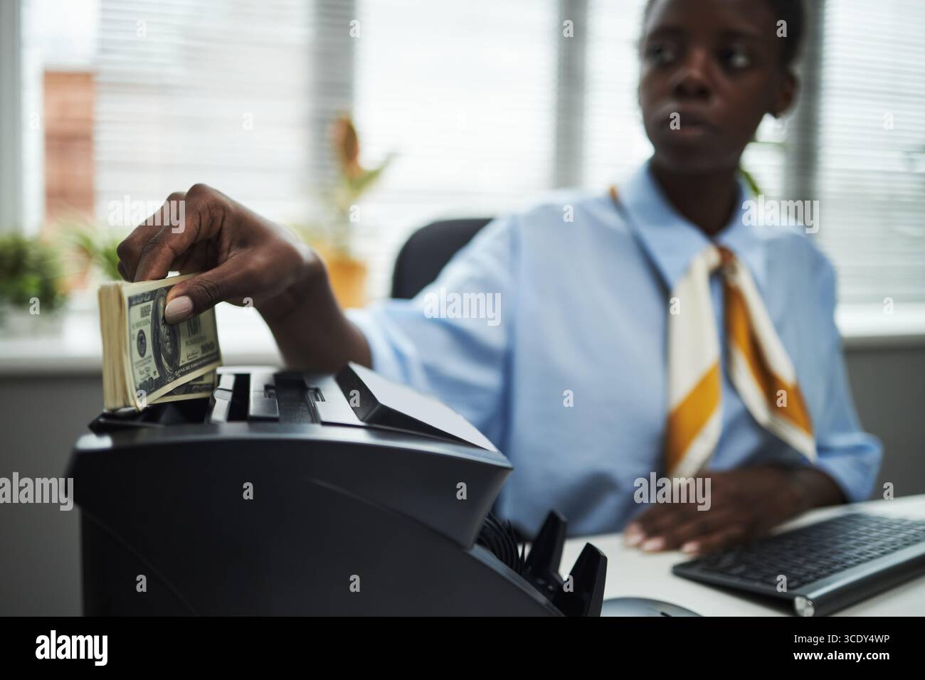 Black female teller inserting stack of US dollar bills into money ...