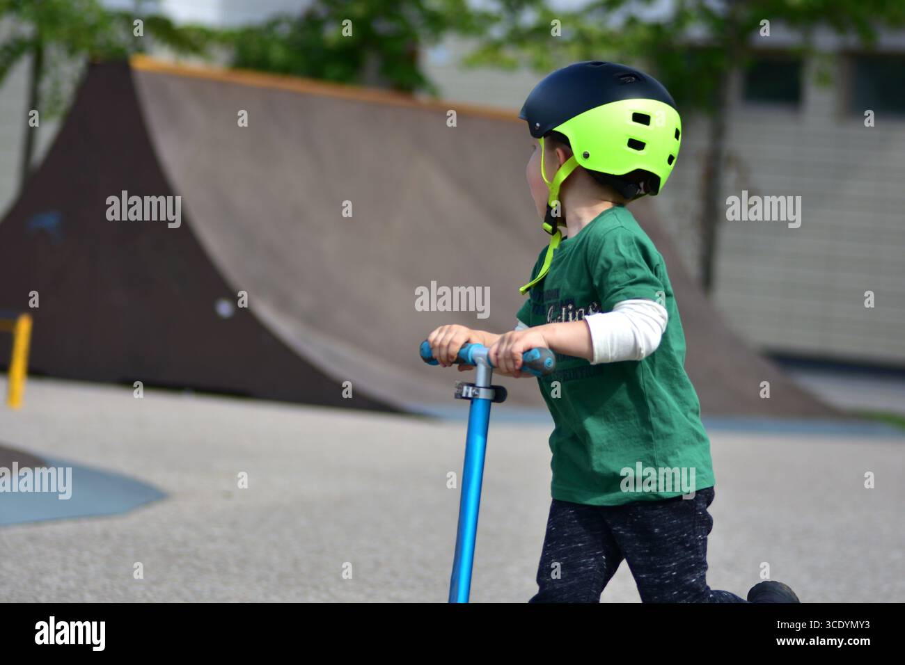 Energetic toddler boy in green shirt and helmet rides his blue three ...