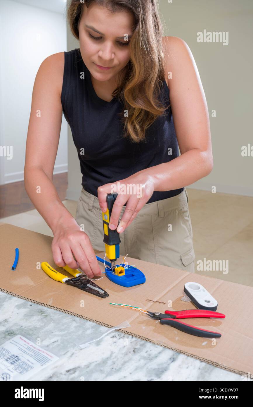 Young woman using a punch down tool to terminate blue Cat-6A ethernet ...