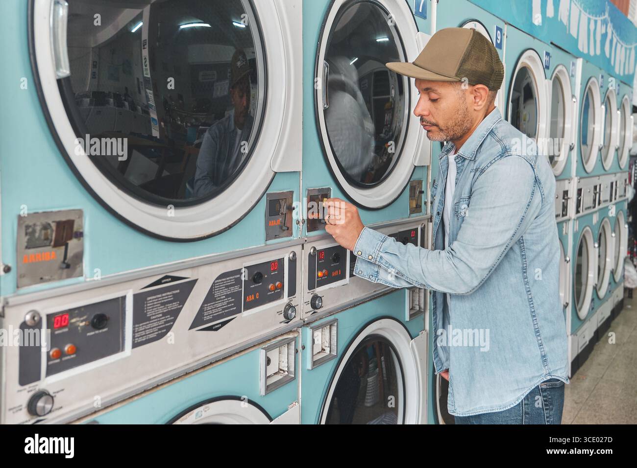 Customer inserting coins into washing machine at laundromat Stock Photo ...