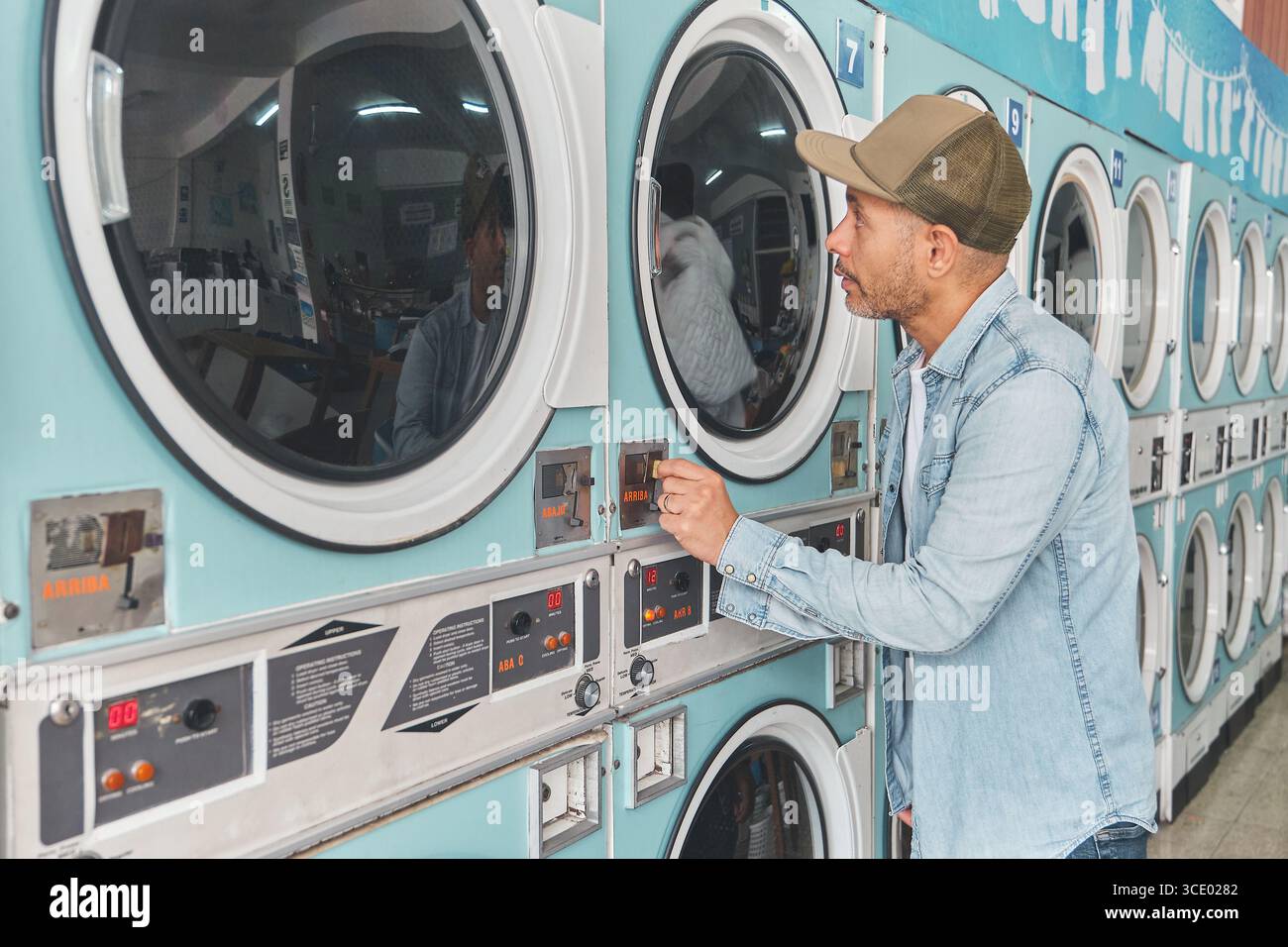 Customer inserting coins into washing machine at laundromat Stock Photo ...