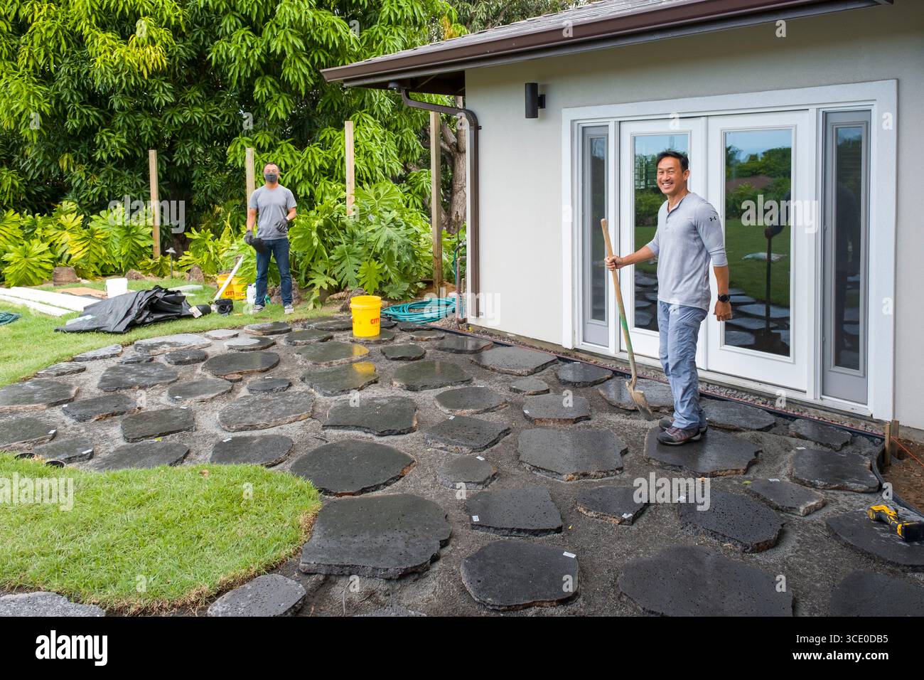 Two construction workers working on placing lava rock landscape pavers ...