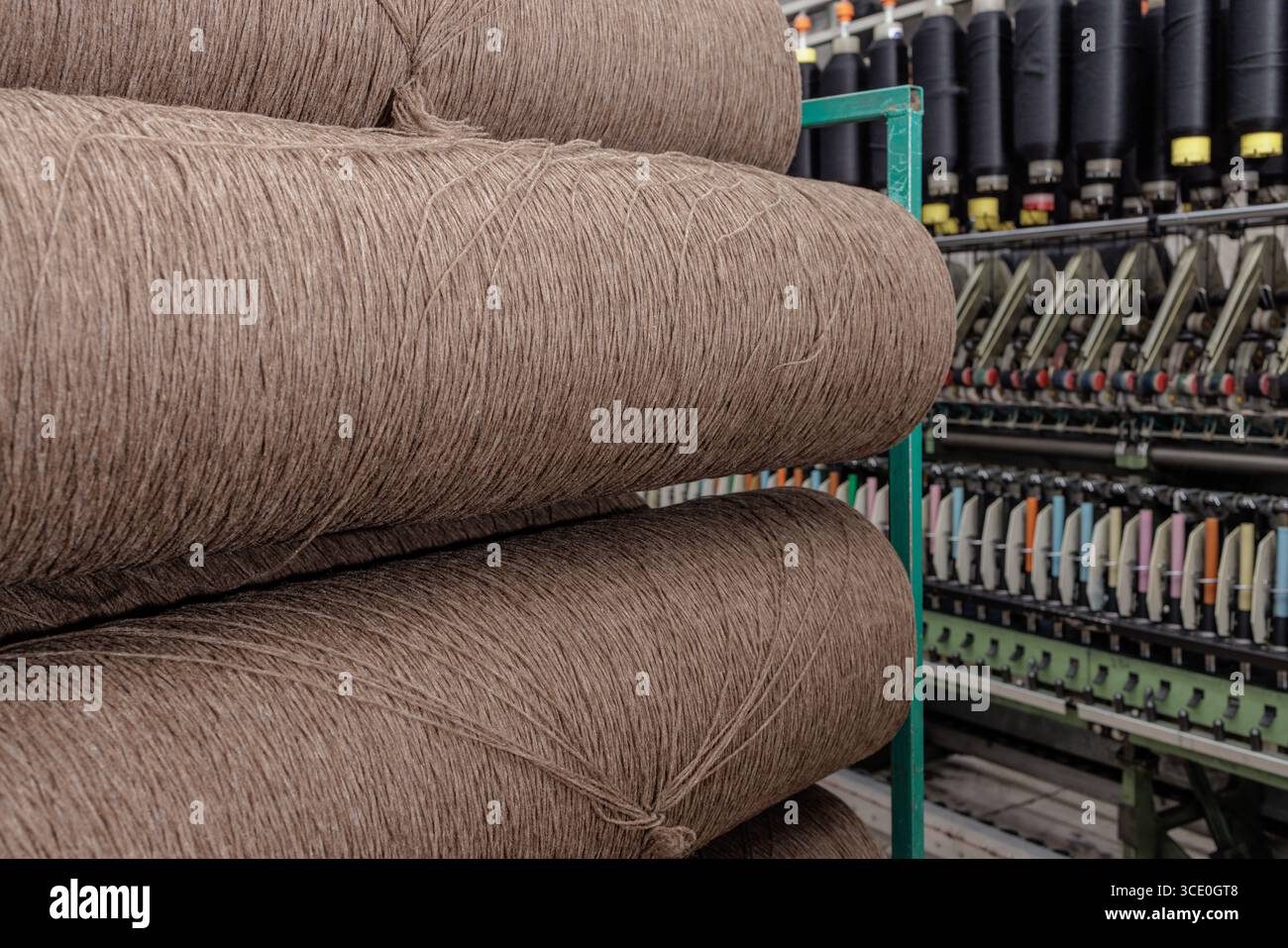 Big yarn rolls stacked next to an operating spinning frame in a textile ...