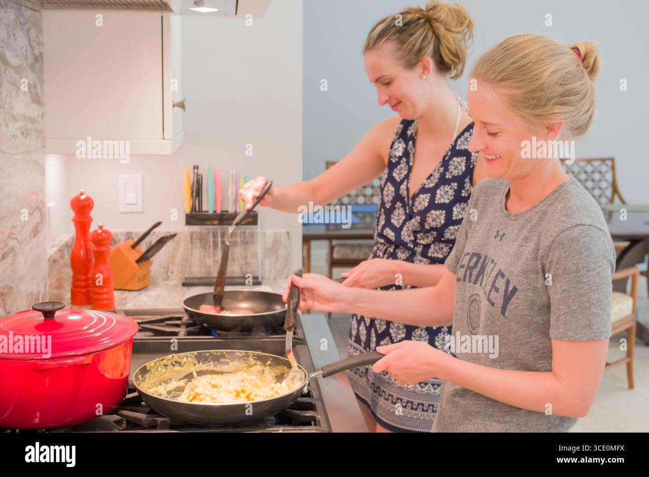 Two young women working in kitchen cooking scrambled eggs and SPAM on ...