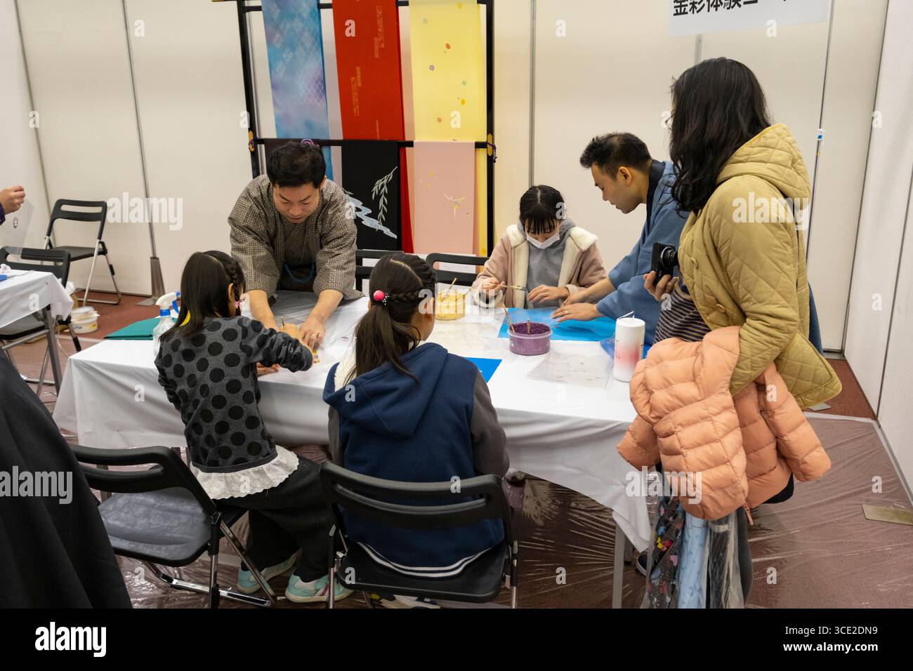 Men wearing kimonos helping children sitting at tables with a hands on ...