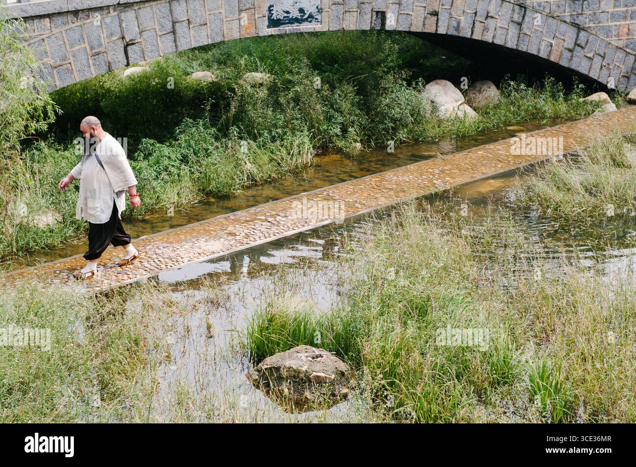 Shaolin Monk Shi De Chao walks on a stone bridge a pond Stock Photo - Alamy