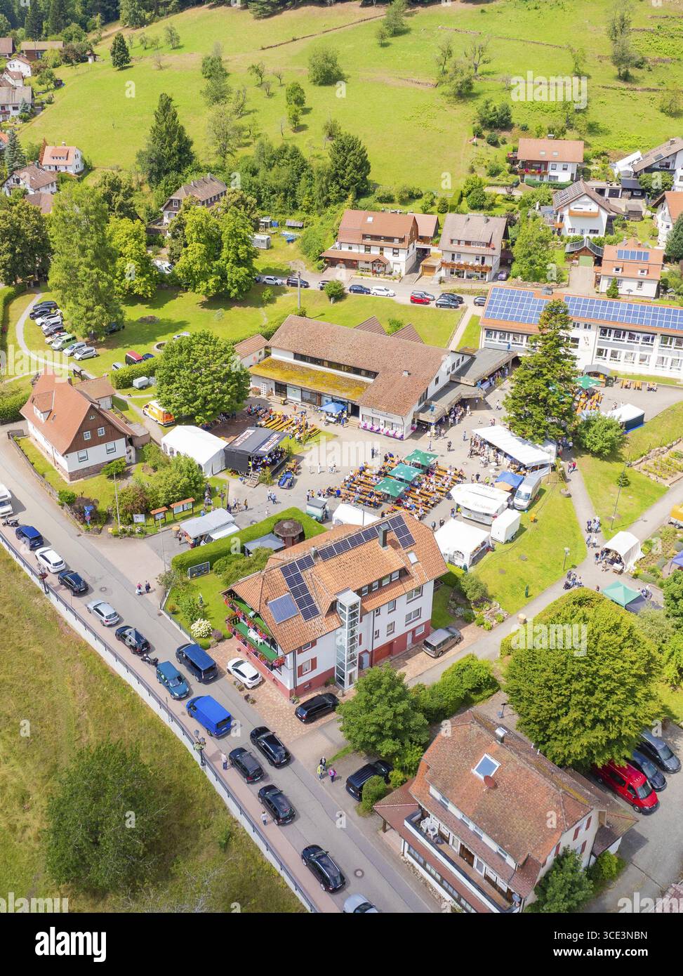 Aerial view of a village festival with numerous cars and solar panels ...