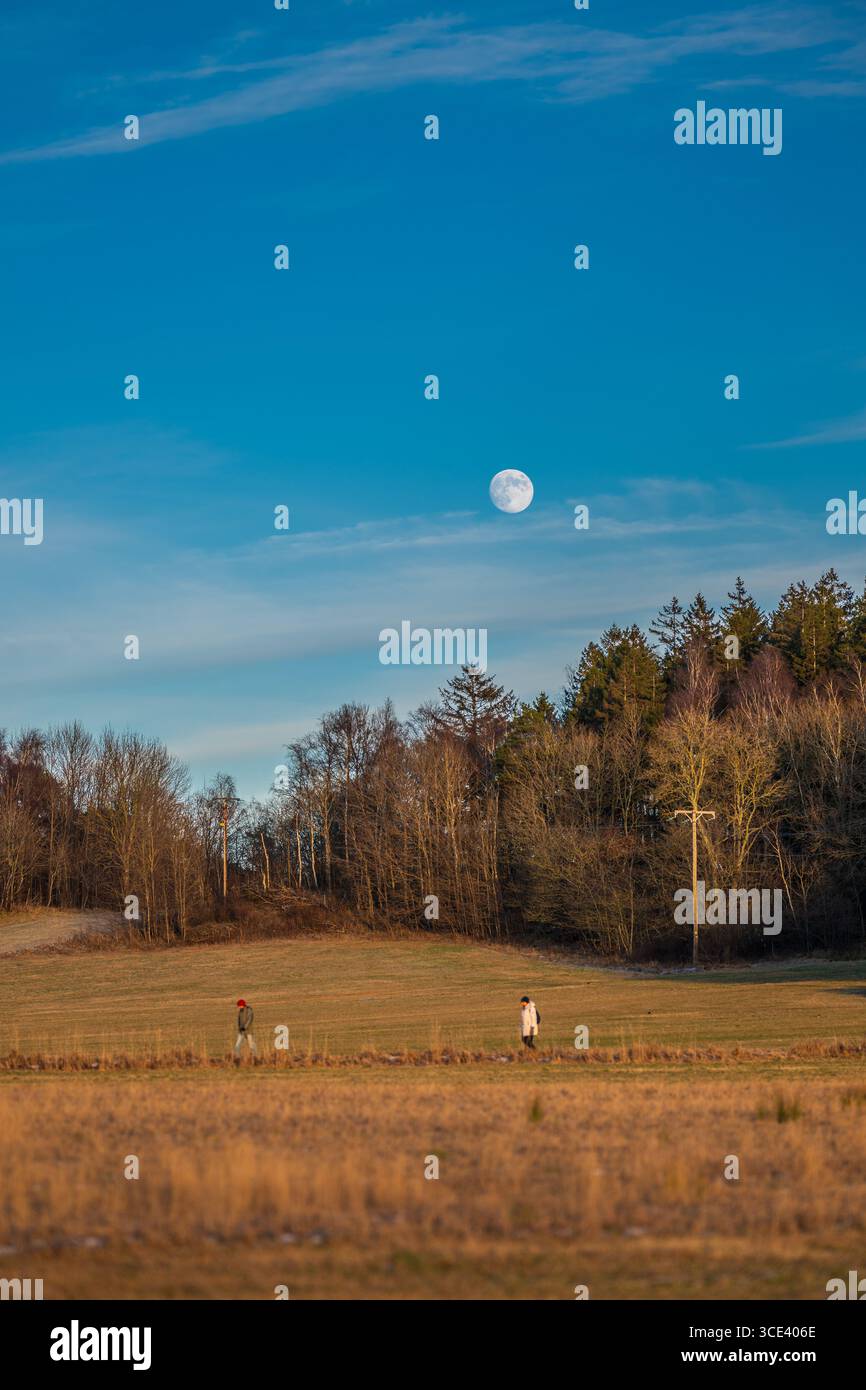 The moon at daytime over people walking across a field Stock Photo - Alamy