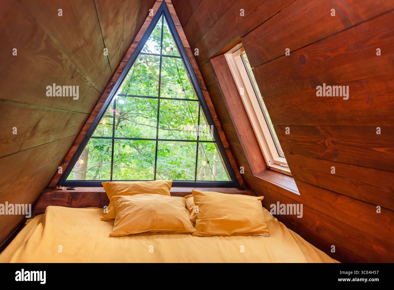 A snug wooden cabin bedroom featuring a triangular window viewing lush ...