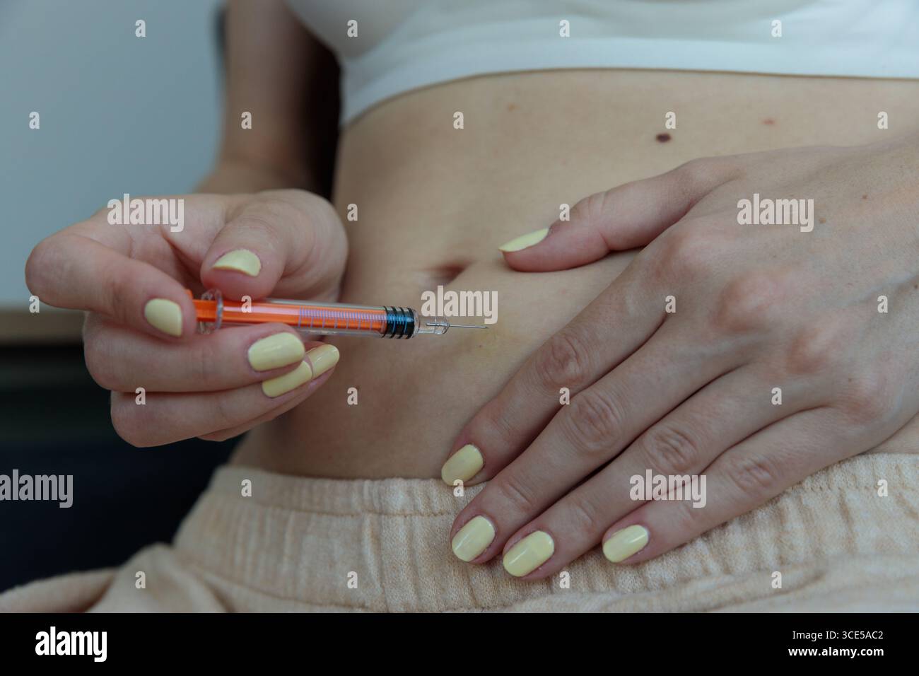 The image shows a close-up of a hand holding a syringe, poised to ...