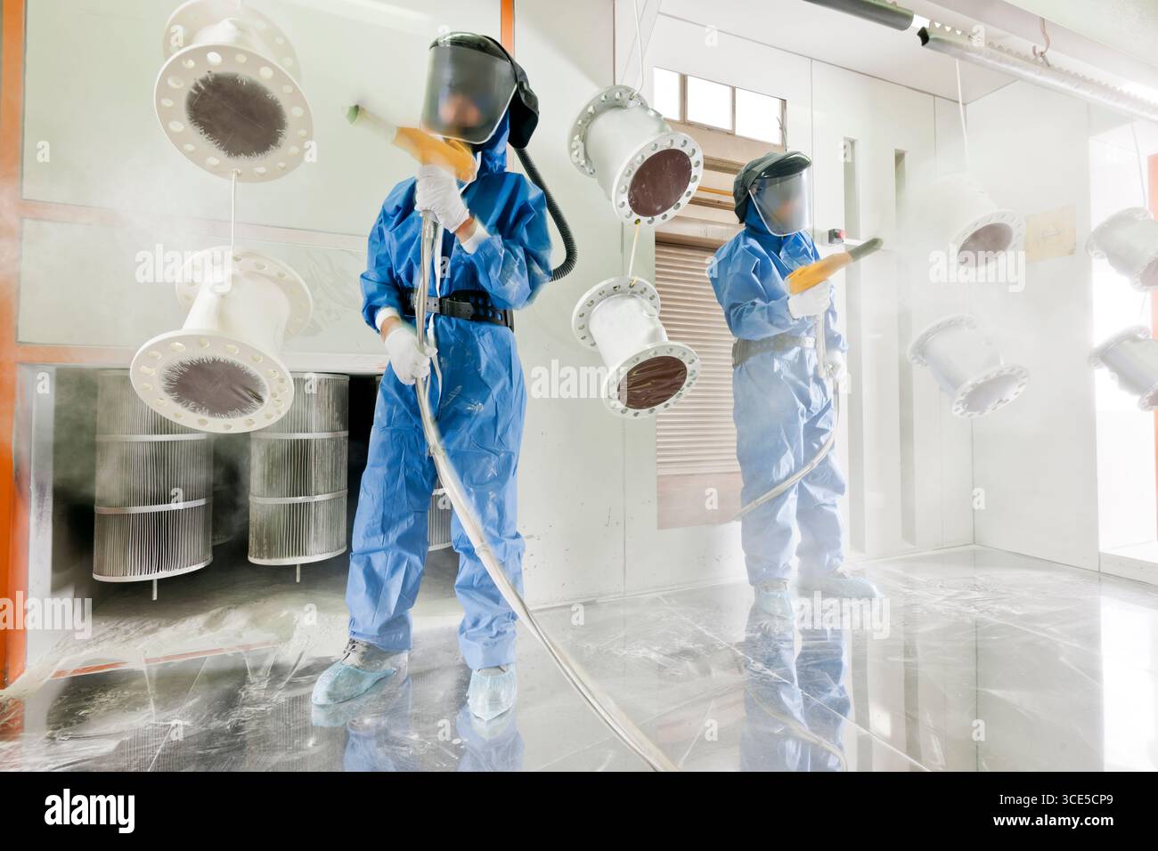 Worker wearing protective wear performing powder coating of metal ...