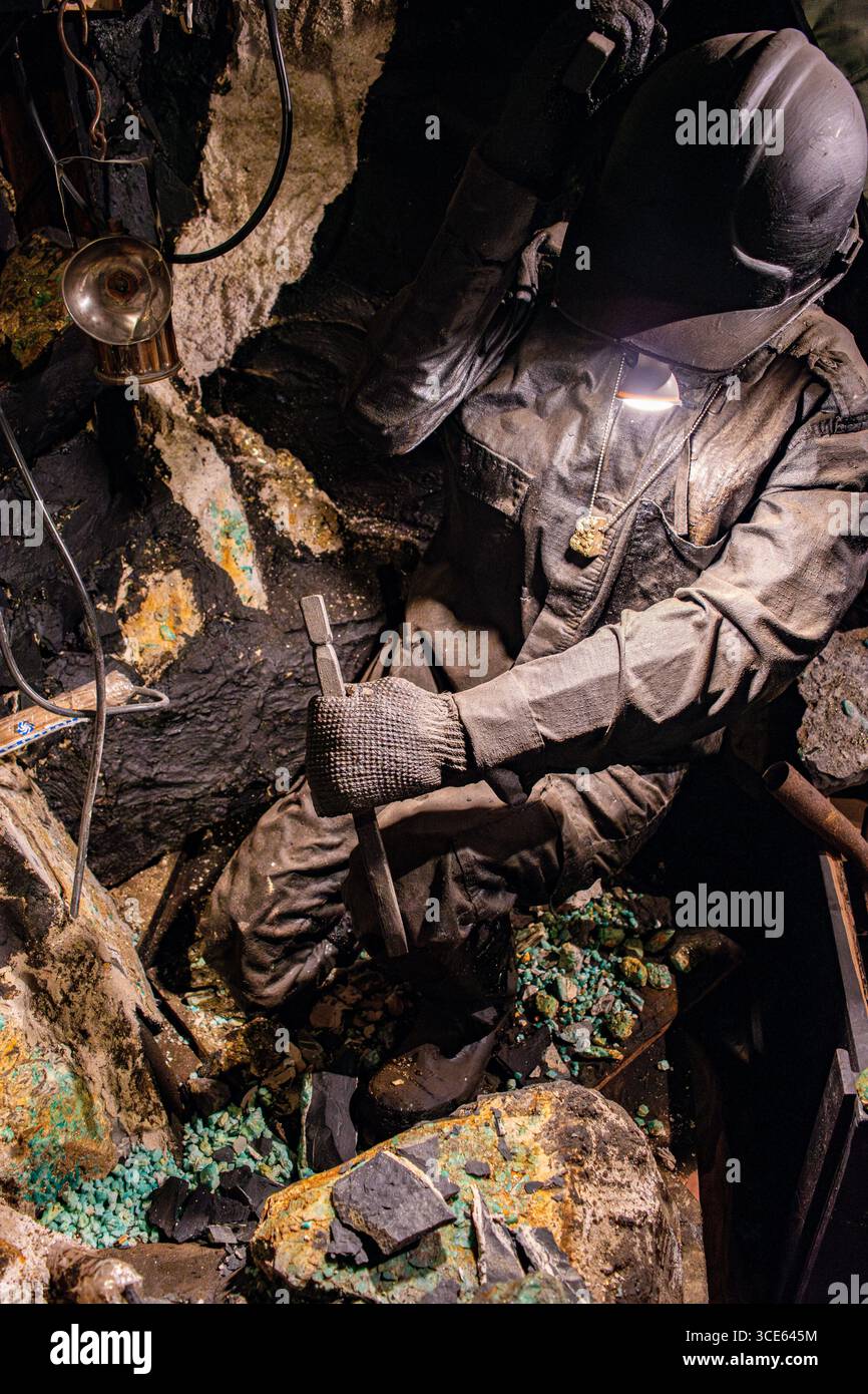 A miner wearing safety gear extracts emeralds in a dark underground ...