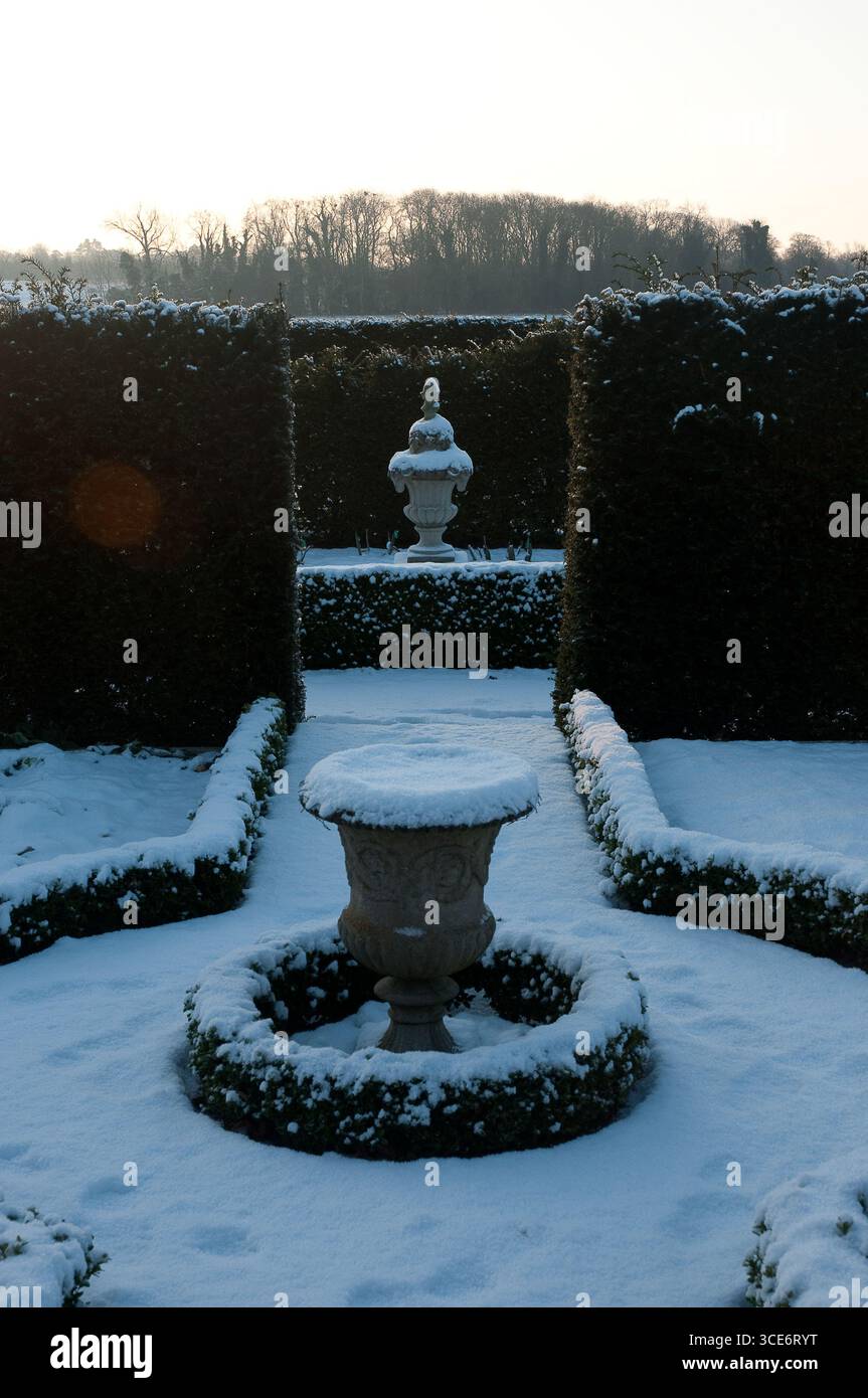 Ornamental garden features snow-covered hedges and a central pedestal ...