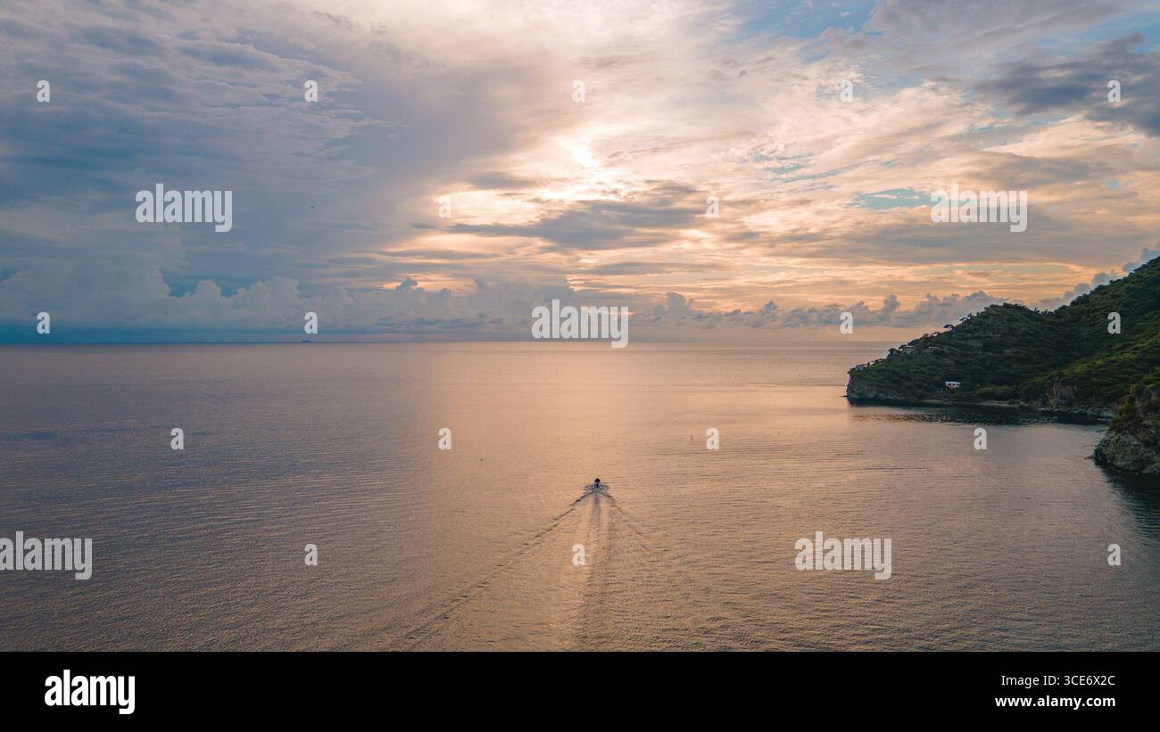 A tranquil sunset view from Santa Marta, Magdalena, Colombia, featuring a boat cruising on calm ...