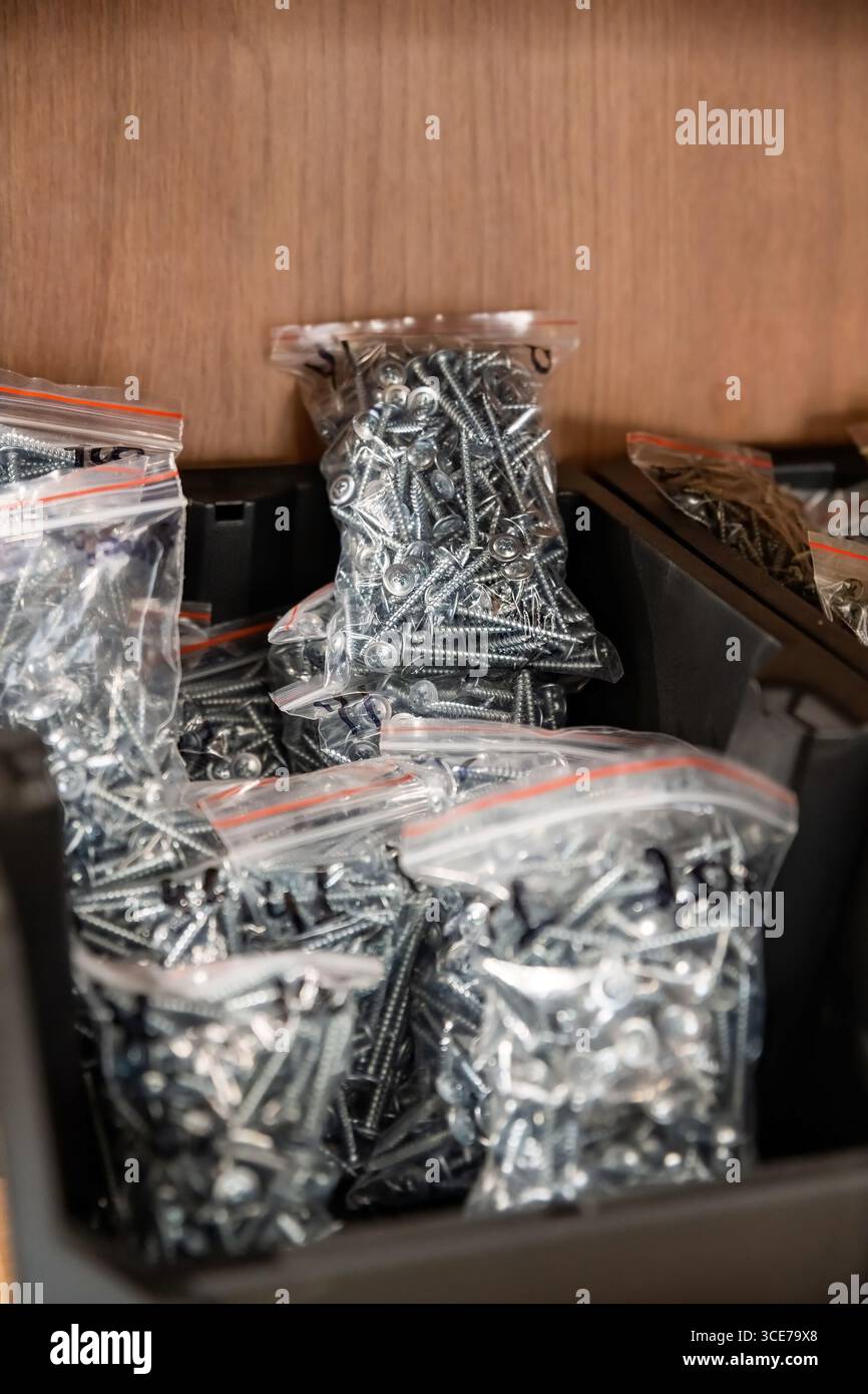 Plastic bags filled with shiny metal screws stored in a black container ...
