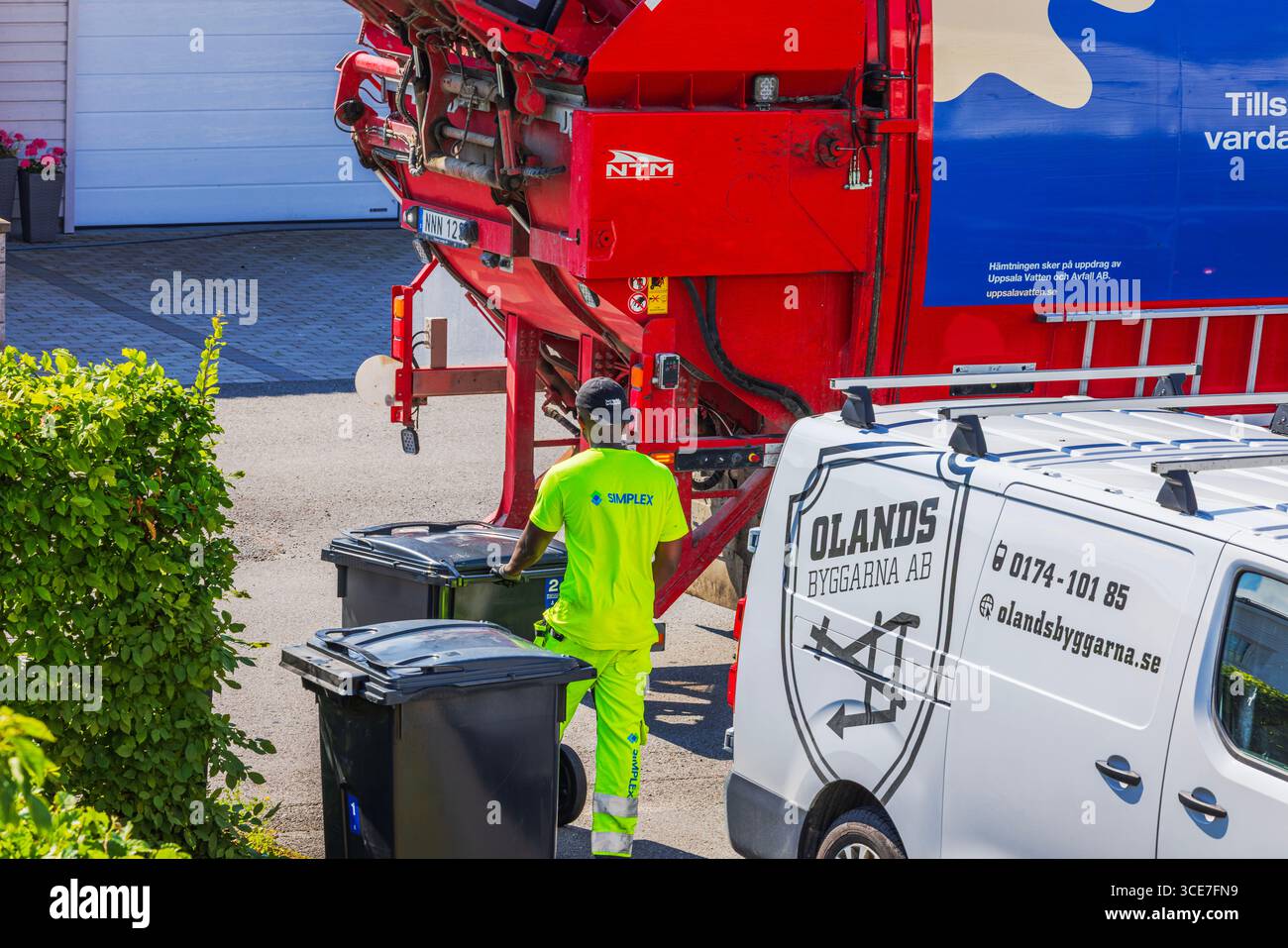 Worker in neon uniform loading garbage bins into red truck against ...
