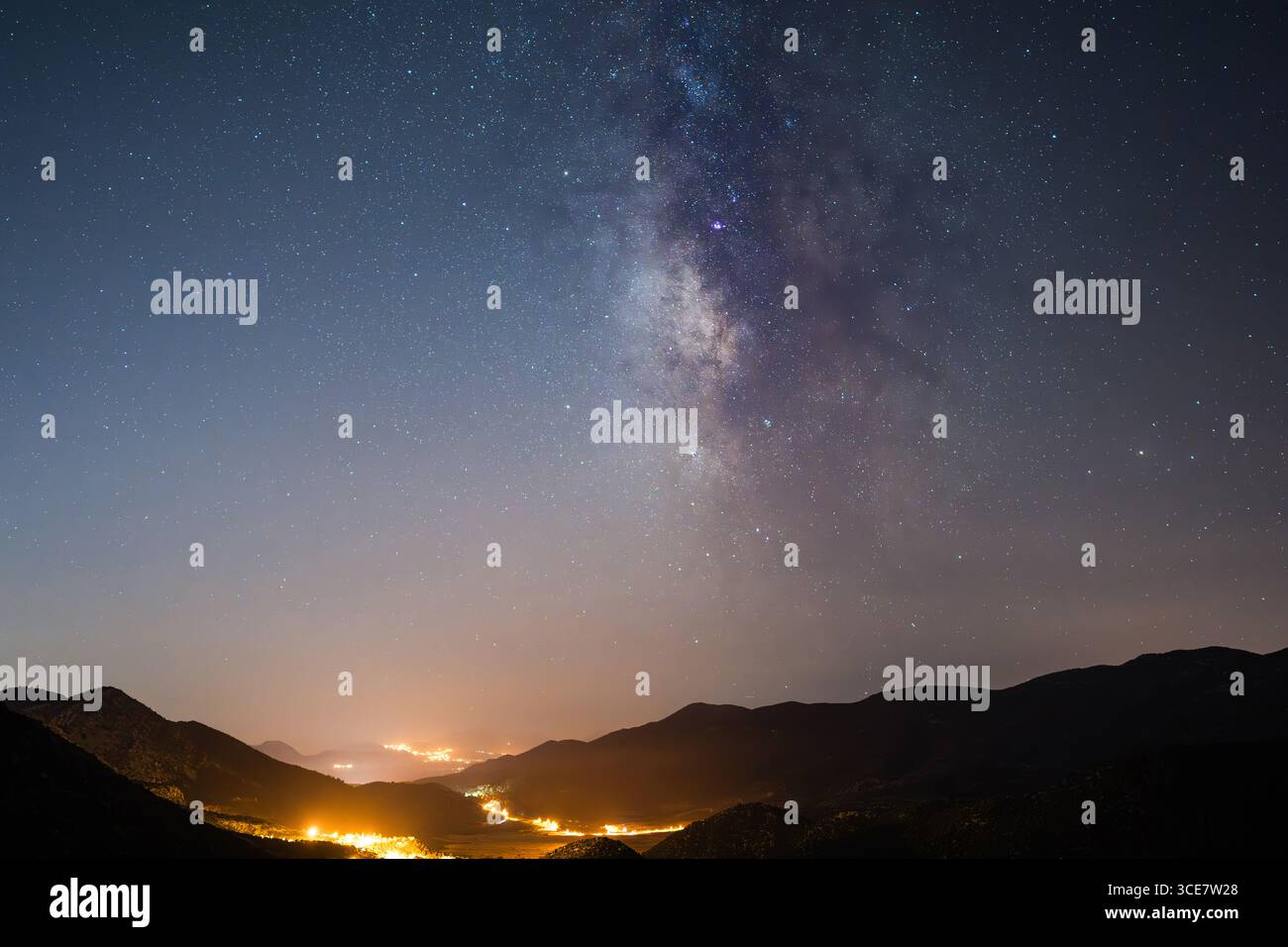 Milky Way galaxy above mountains and glowing village lights at night ...