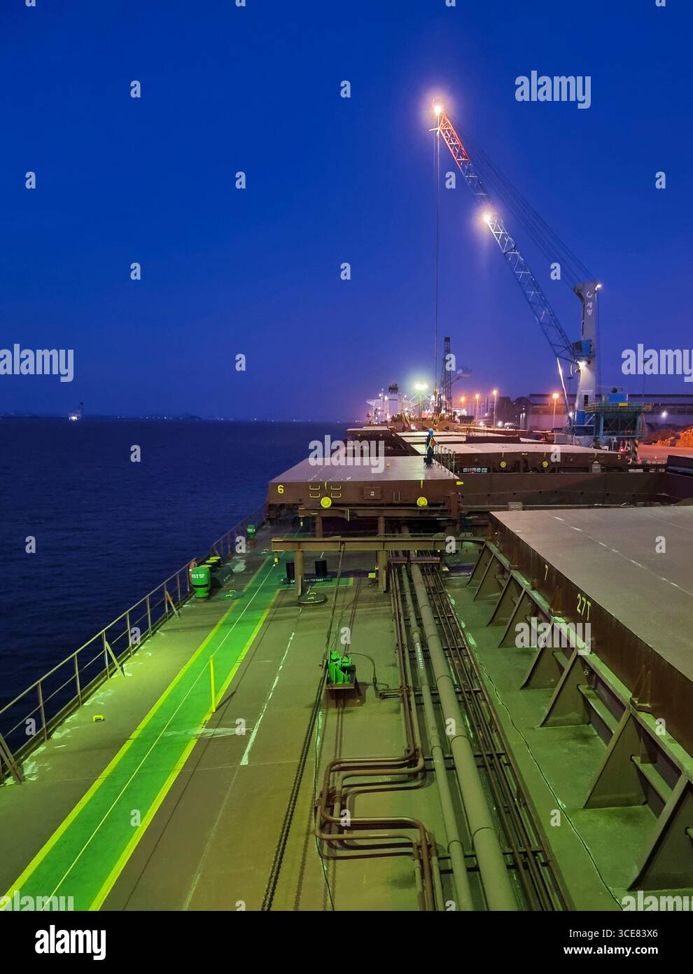 Cargo ship with open hatches and crane loading cargo at twilight ...