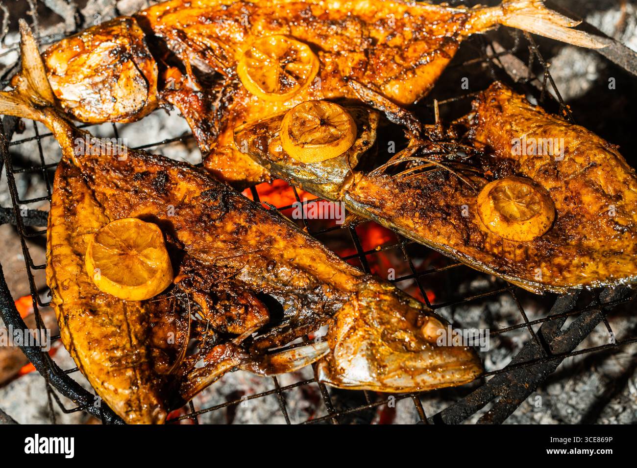 Marinated fish grilled over hot charcoal with lemon slices on top Stock ...