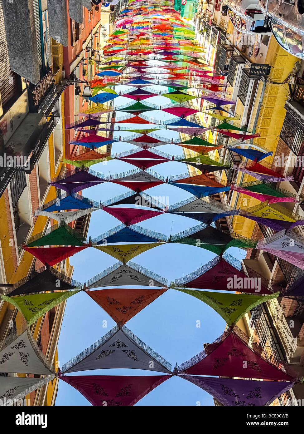 Rows of colorful fabric canopies are strung above a narrow street ...