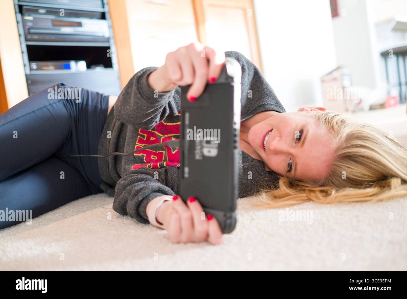 Young woman laying on carpet at home playing with a Nintendo Switch ...