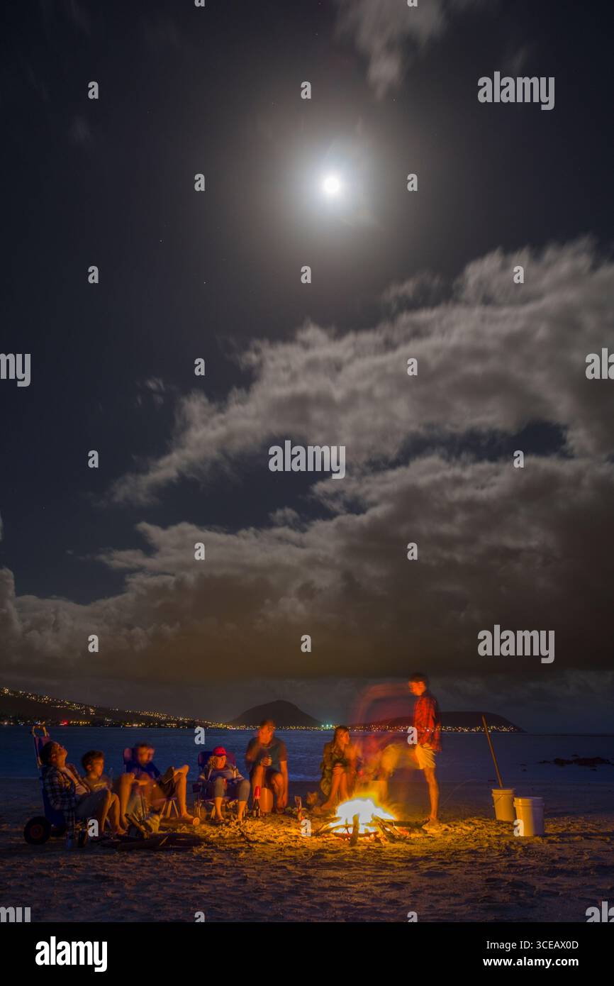 Family and friends enjoying a fire on sandbar at night under a full ...