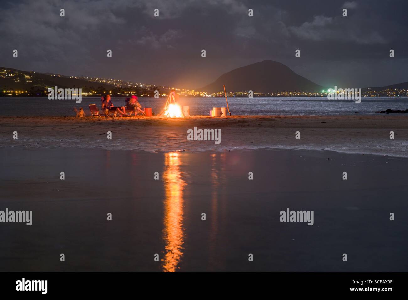 Family and friends enjoying a fire on sandbar at night under a full ...
