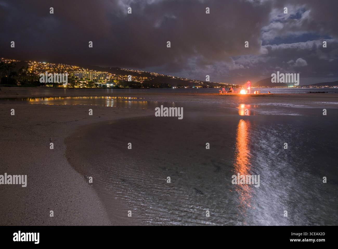 Family and friends enjoying a fire on sandbar at night under a full ...