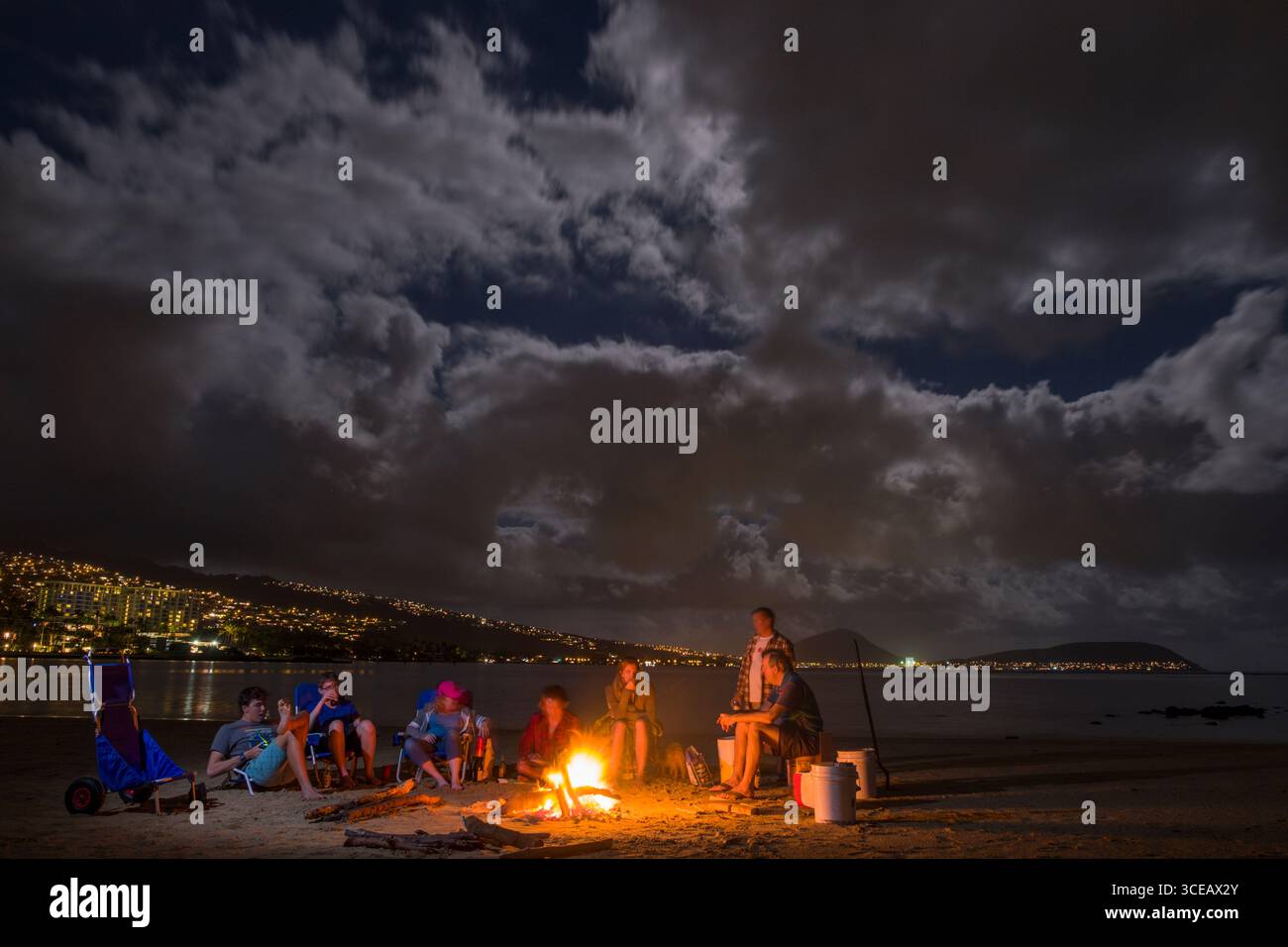 Family and friends enjoying a fire on sandbar at night under a full ...
