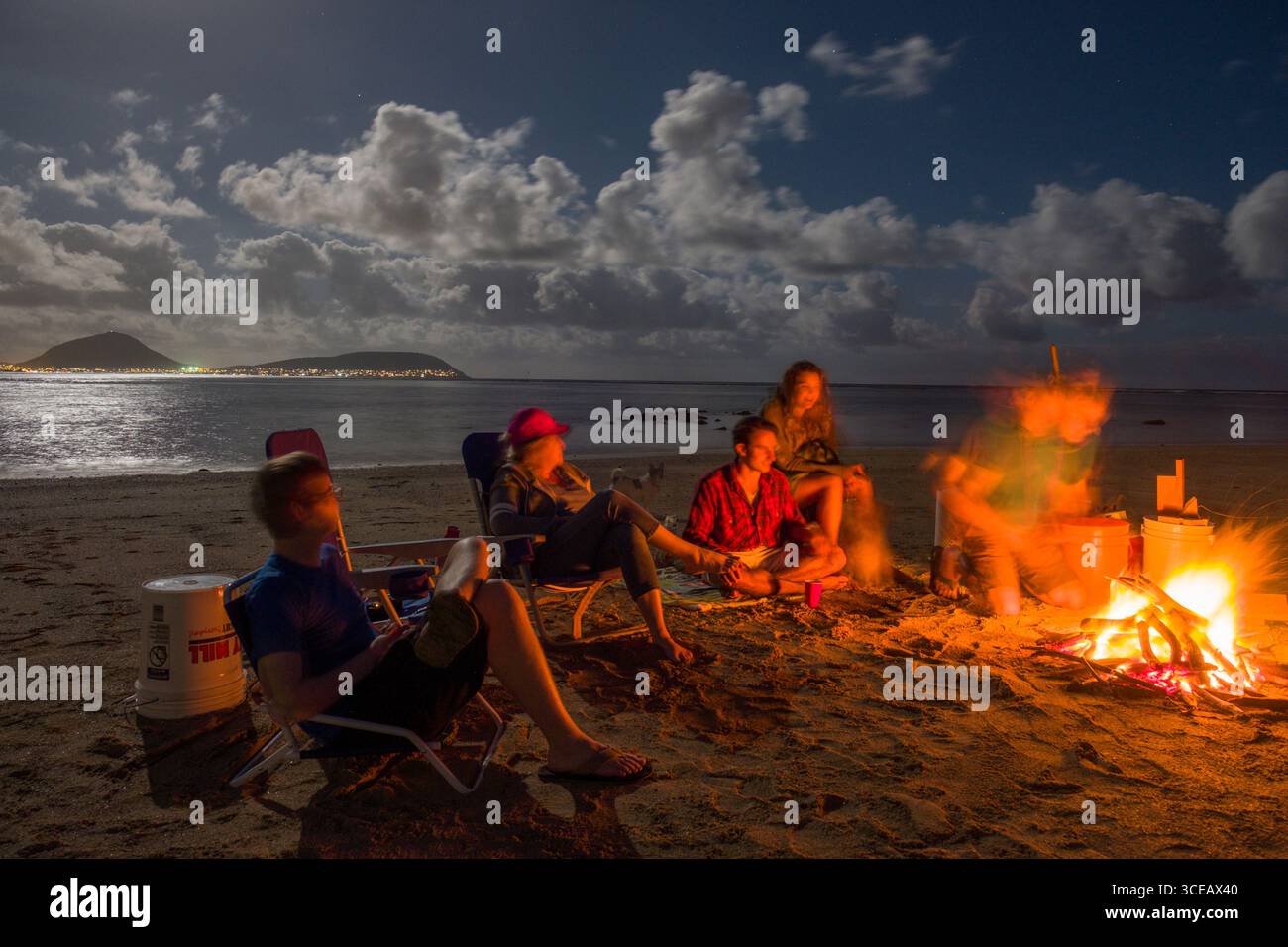 Family and friends enjoying a fire on sandbar at night under a full ...