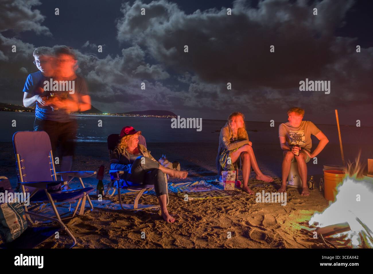 Family and friends enjoying a fire on sandbar at night under a full ...