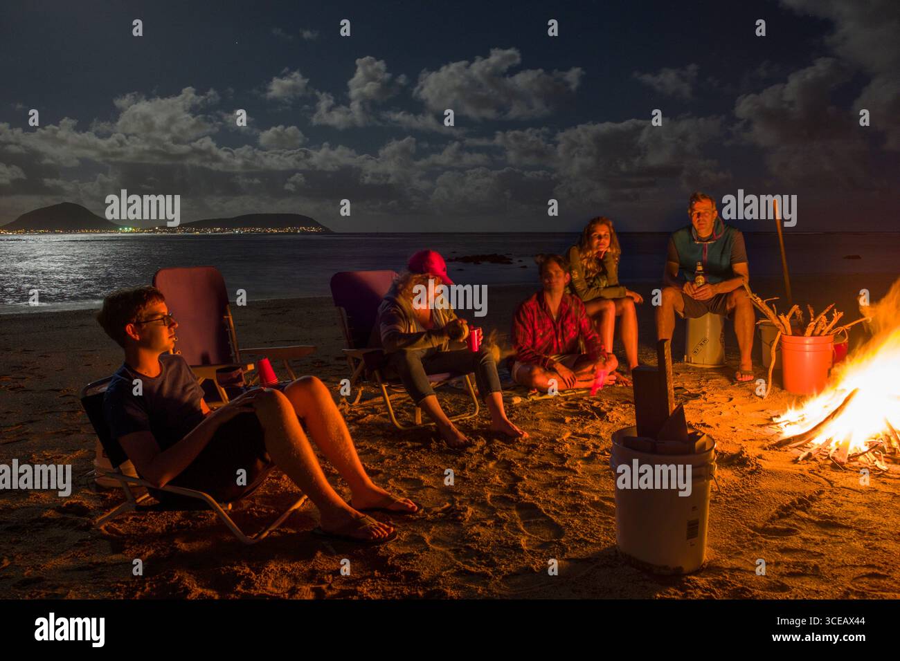 Family and friends enjoying a fire on sandbar at night under a full ...