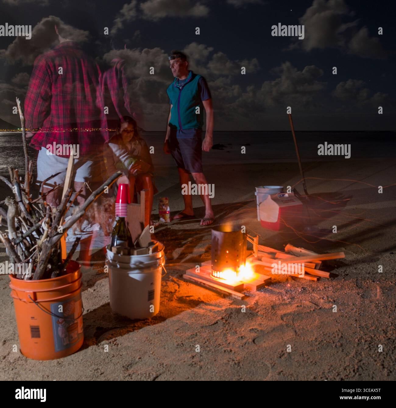 Family and friends enjoying a fire on sandbar at night under a full ...