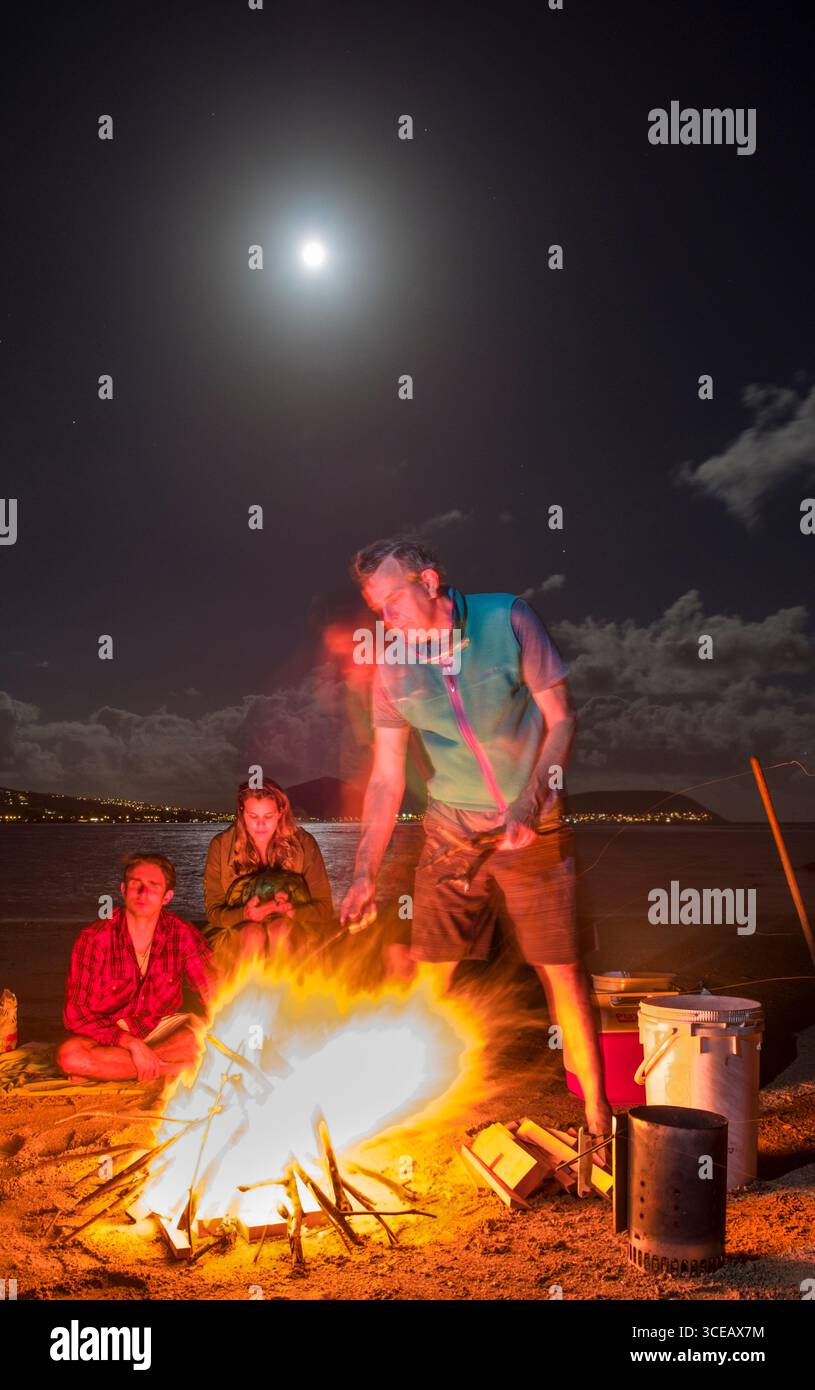 Family and friends enjoying a fire on sandbar at night under a full ...