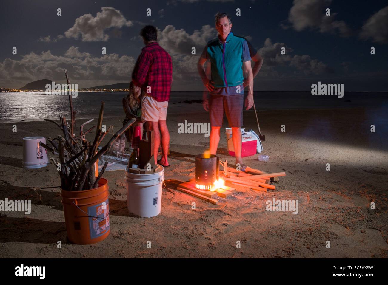 Family and friends enjoying a fire on sandbar at night under a full ...