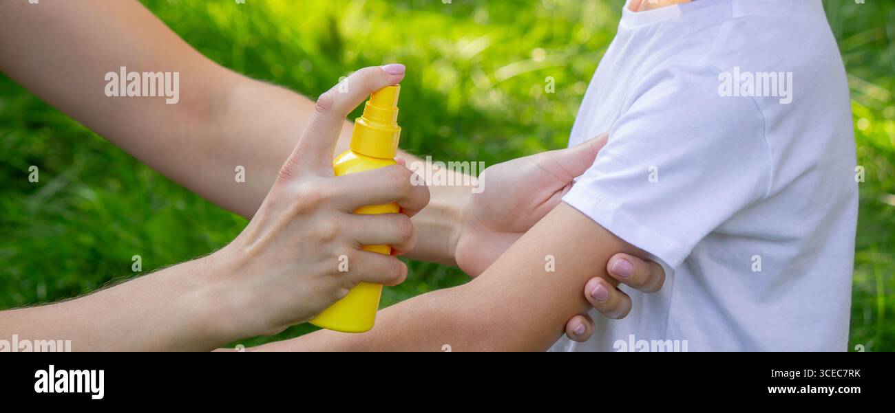 Mother spraying mosquito repellent on child hand outdoors in summer ...