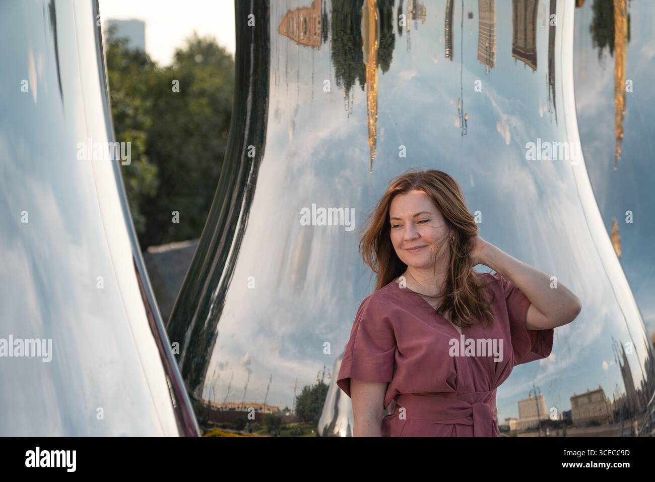 Woman in a rose dress poses beside giant reflective matryoshka ...