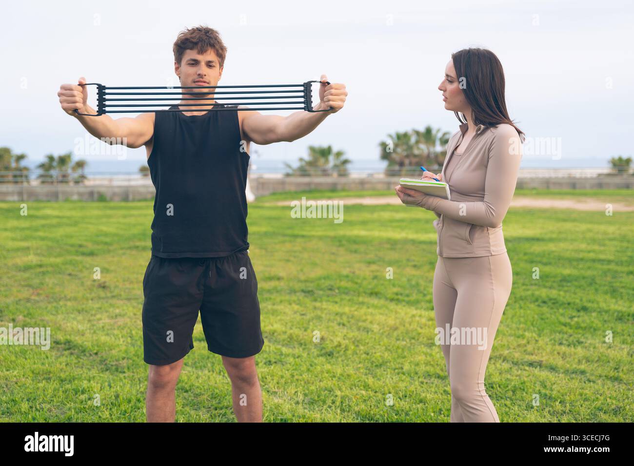 Sporty man training with resistance band while female coach takes notes ...