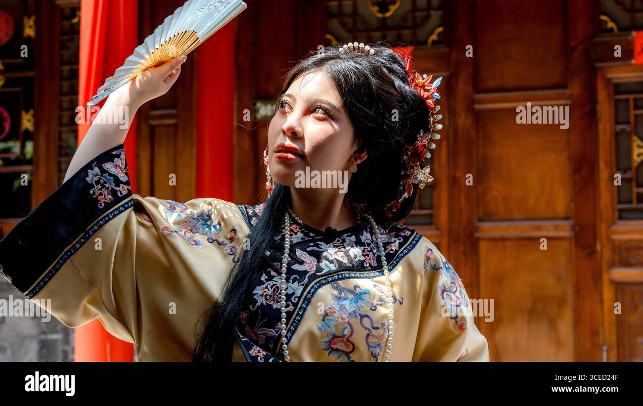 A young woman dressed in traditional Qing Dynasty attire poses with a ...