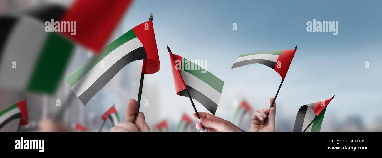 Arab Emirates flags in their hands on a blurred urban background. The ...
