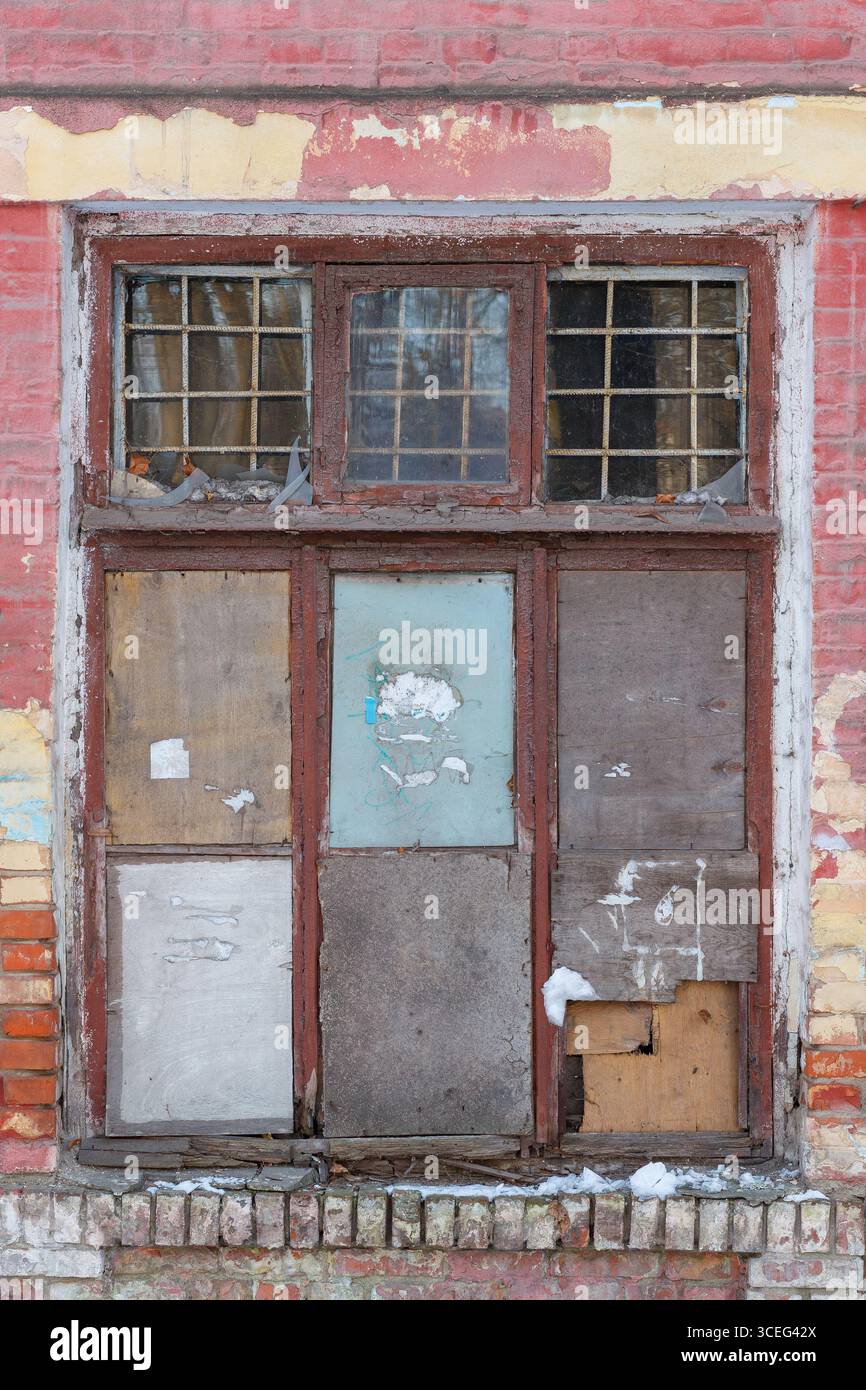 Weathered red brick wall with an old window covered by wooden boards ...