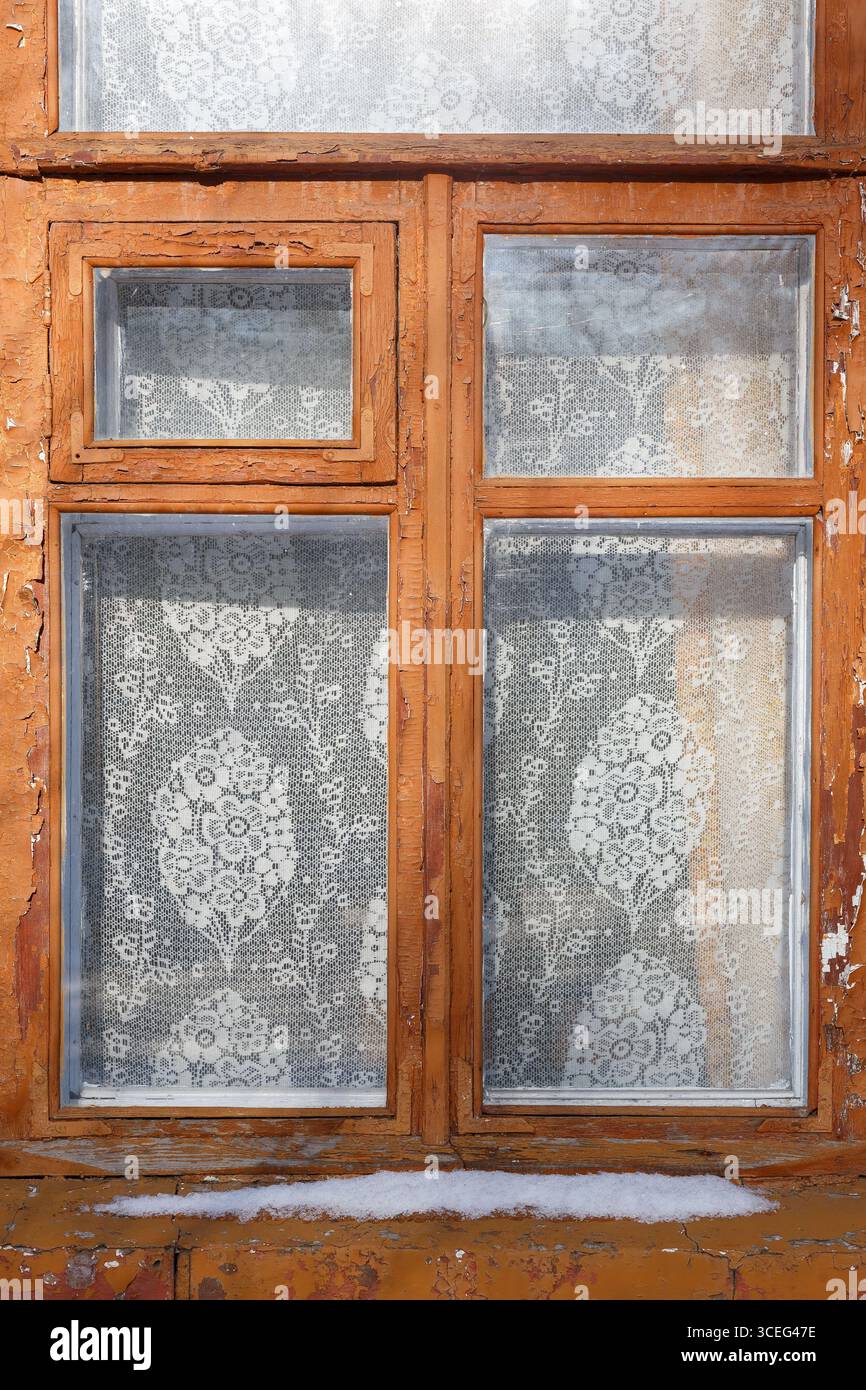 Close-up of an old wooden-framed window with peeling paint, lace ...