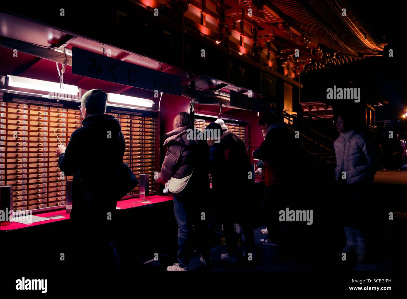 People drawing omikuji fortunes under the warm temple lights of Sensō ...