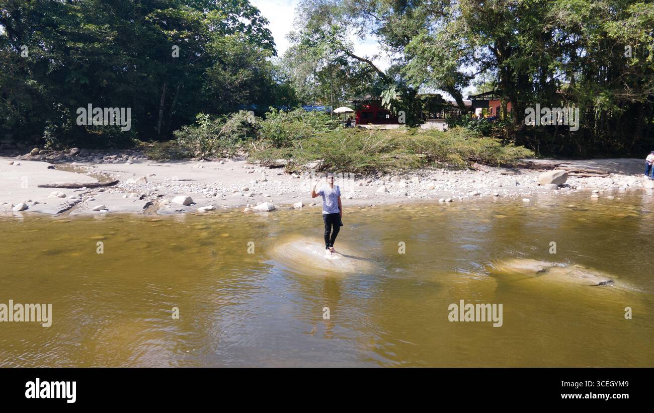 A man stands in a shallow river in Putumayo, Colombia, surrounded by ...