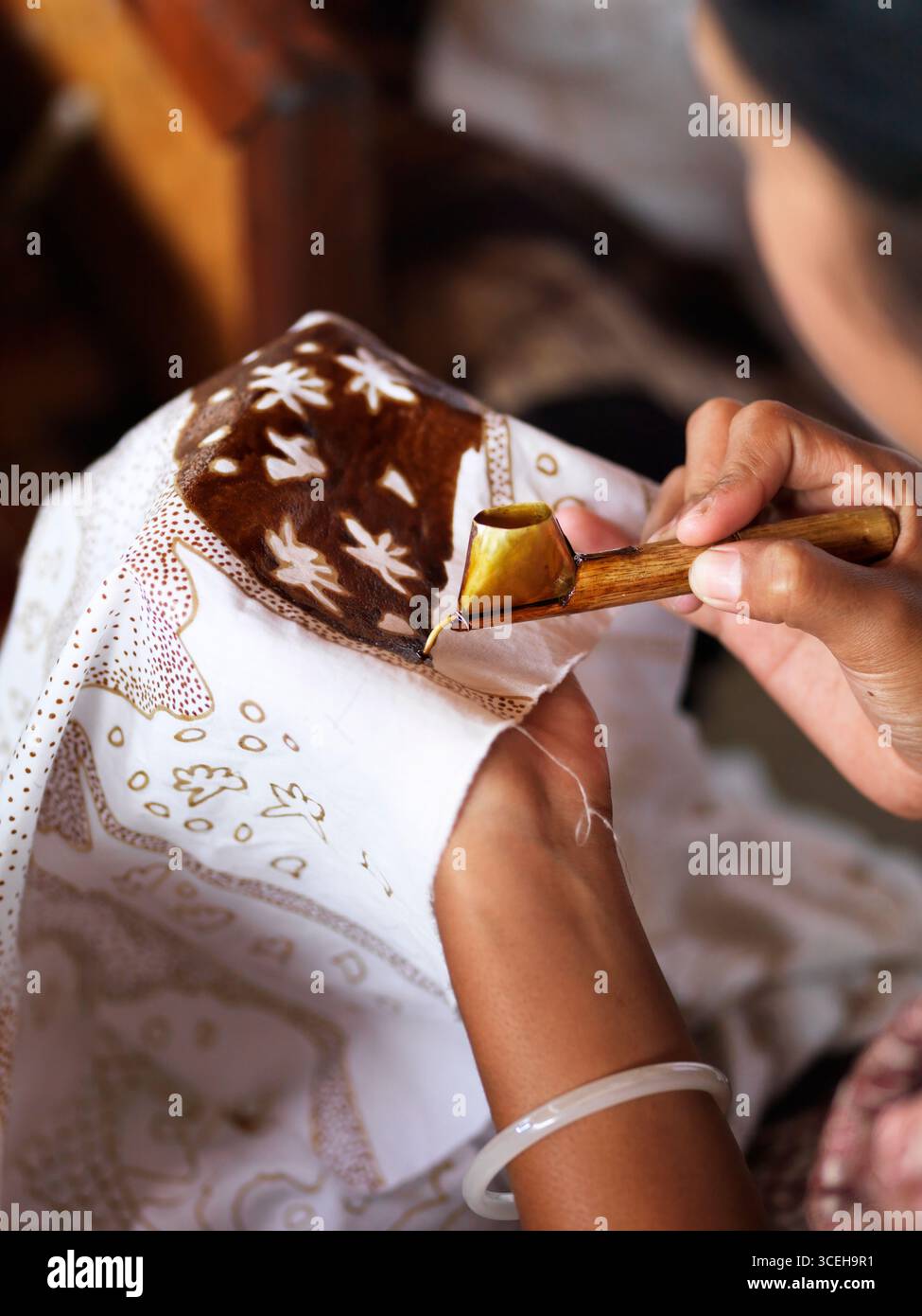 A woman applies liquid wax to a fabric with a canting, which is used in ...
