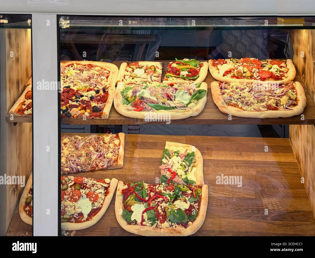 Display of rectangular pizzas with various toppings inside glass ...