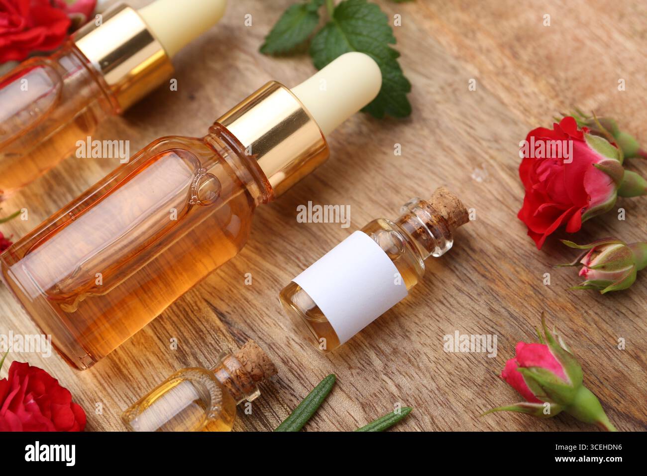 Bottles of essential oils, red roses and herbs on wooden table, closeup ...