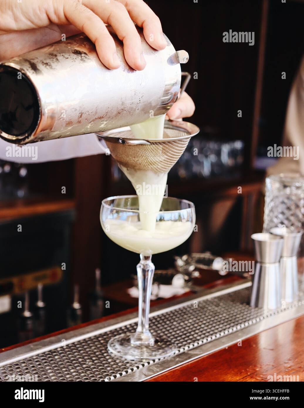 Bartender pouring a freshly shaken cocktail through a strainer into a ...