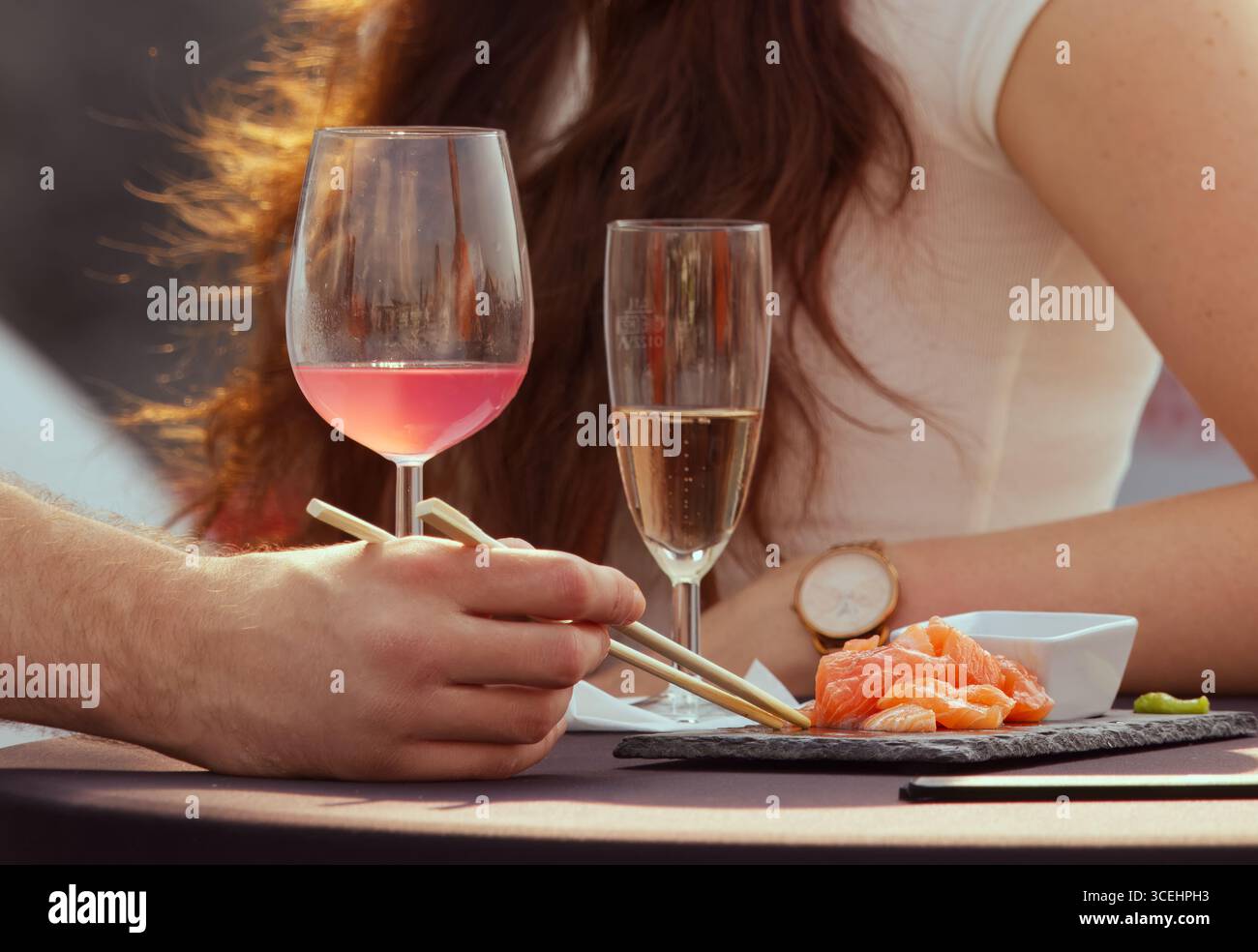Close-up of couple enjoying sushi with chopsticks and glasses of wine ...